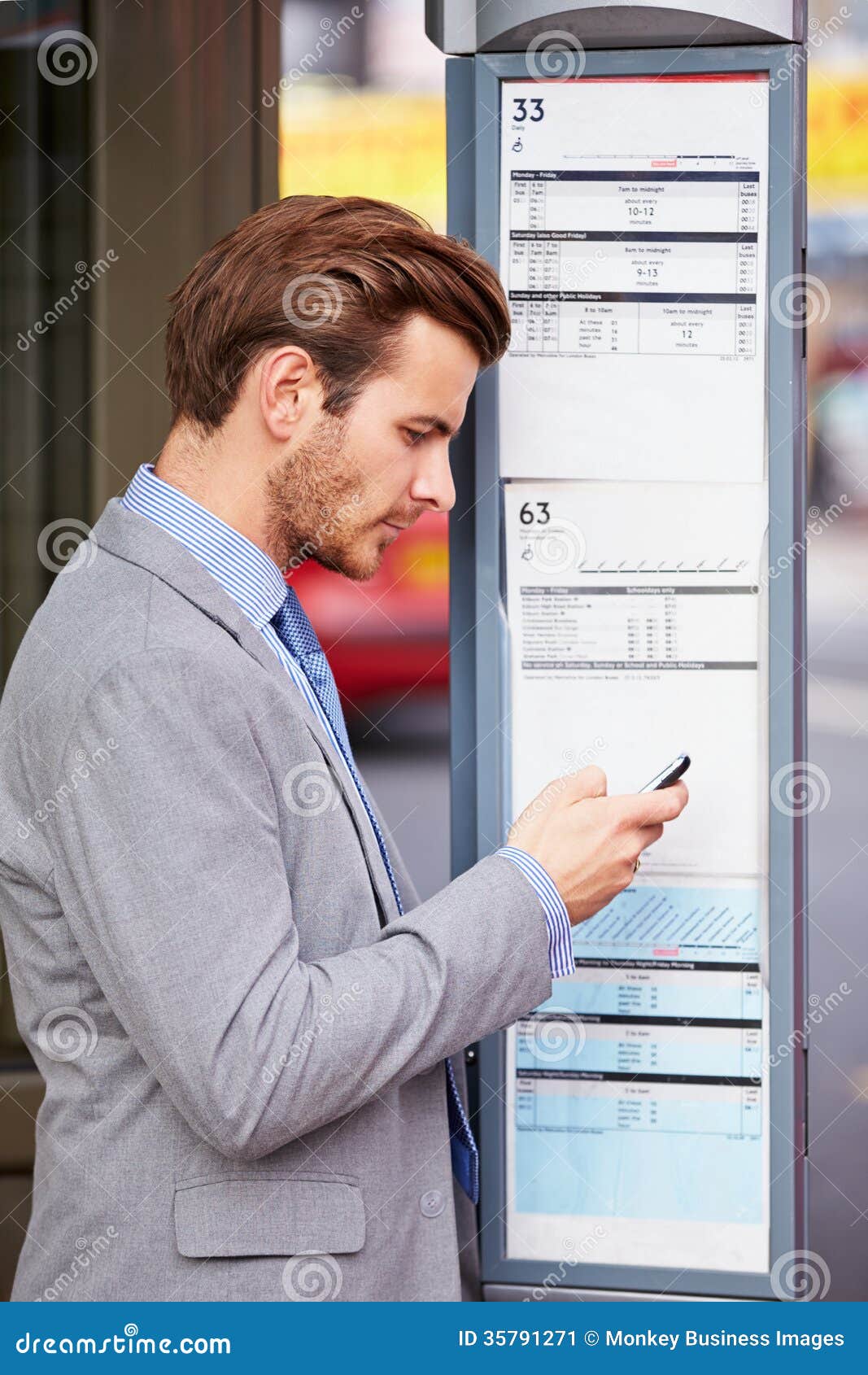 Businessman at Bus Stop with Mobile Phone Reading Timetable Stock Image ...