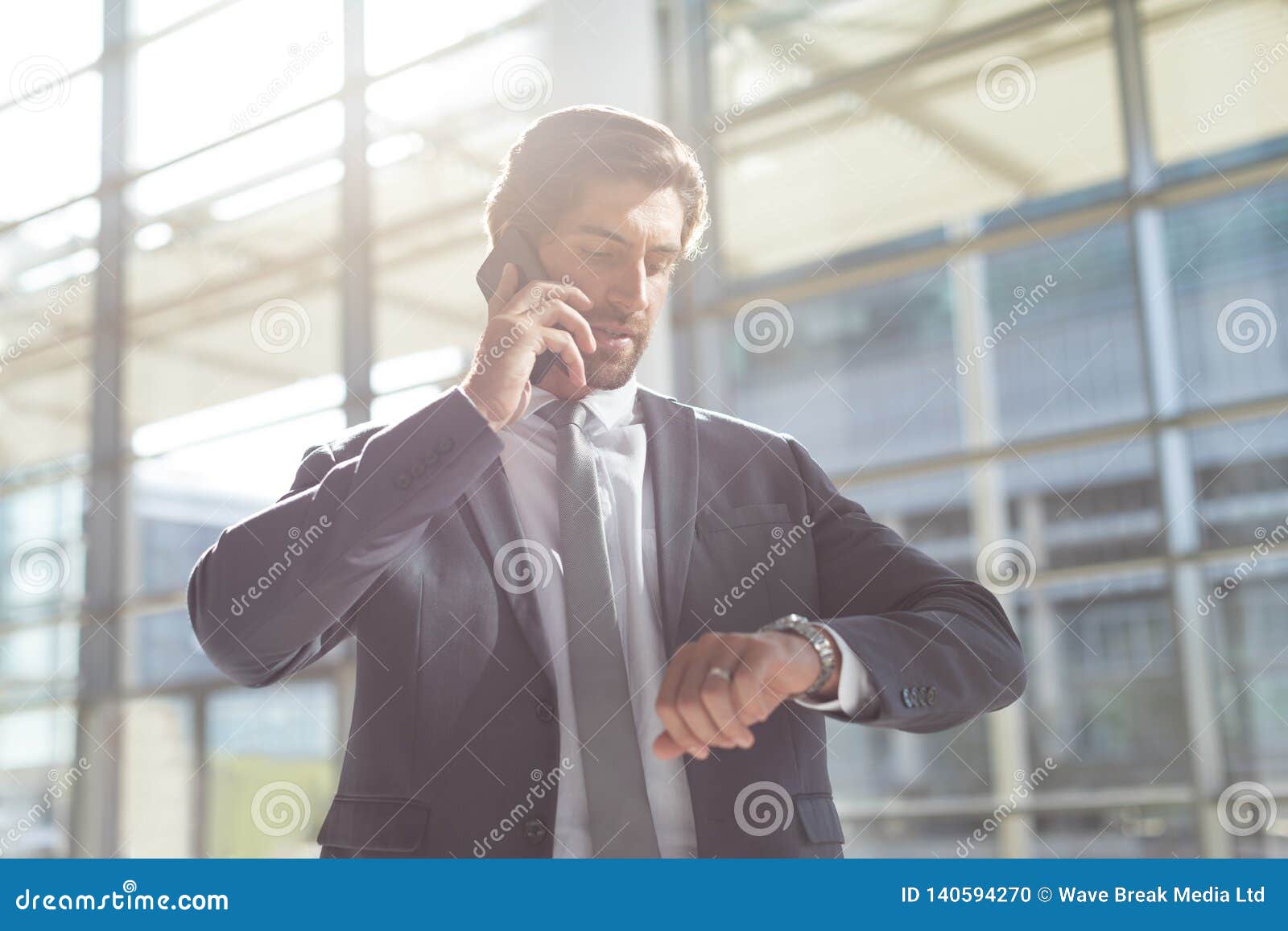 Businessman Checking Time while Talking on Mobile Phone in Lobby Office ...