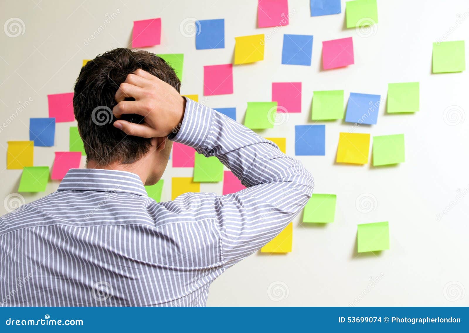 Businessman Looking at Wall of Sticky Notes with Hands Behind Head ...