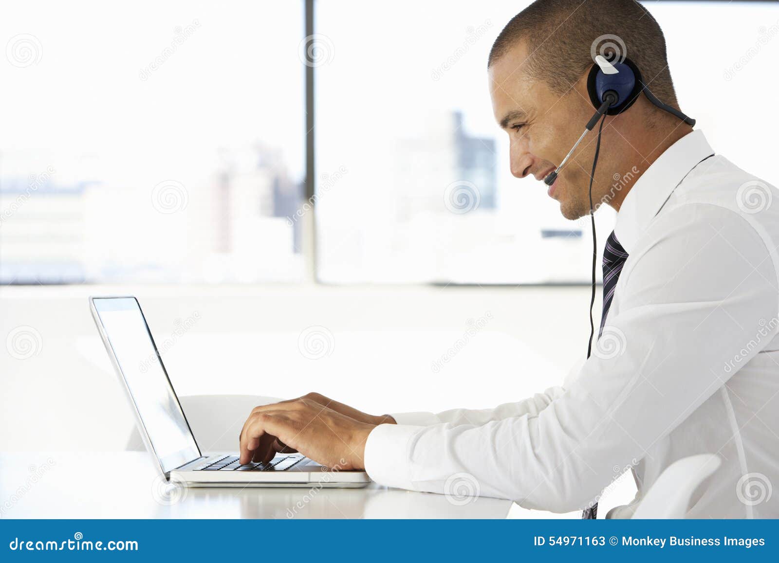 Businessman Sitting at Desk in Office Using Laptop Wearing Headset ...