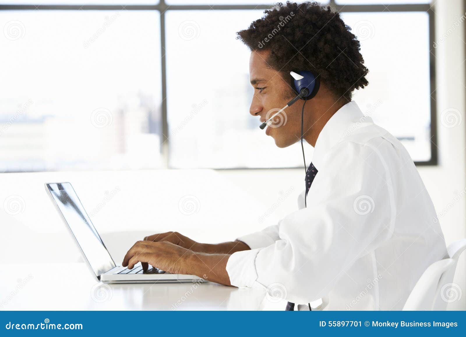 Businessman Sitting at Desk in Office Using Laptop Wearing Headset ...
