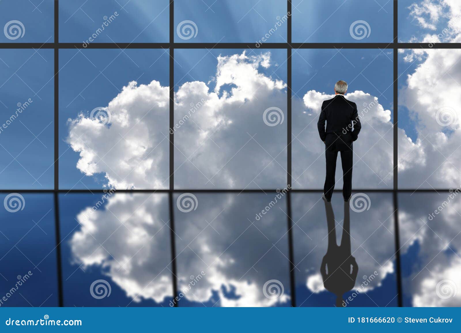 Businessman Standing in Front of a Large Bank of Windows with Clouds ...