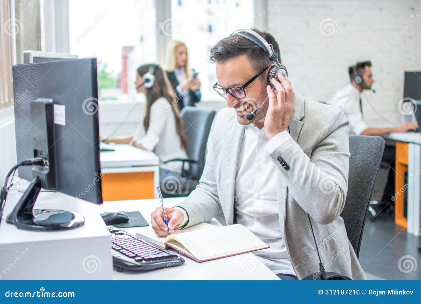 Businessman Taking Notes while Talking with Customer Using Headphones ...