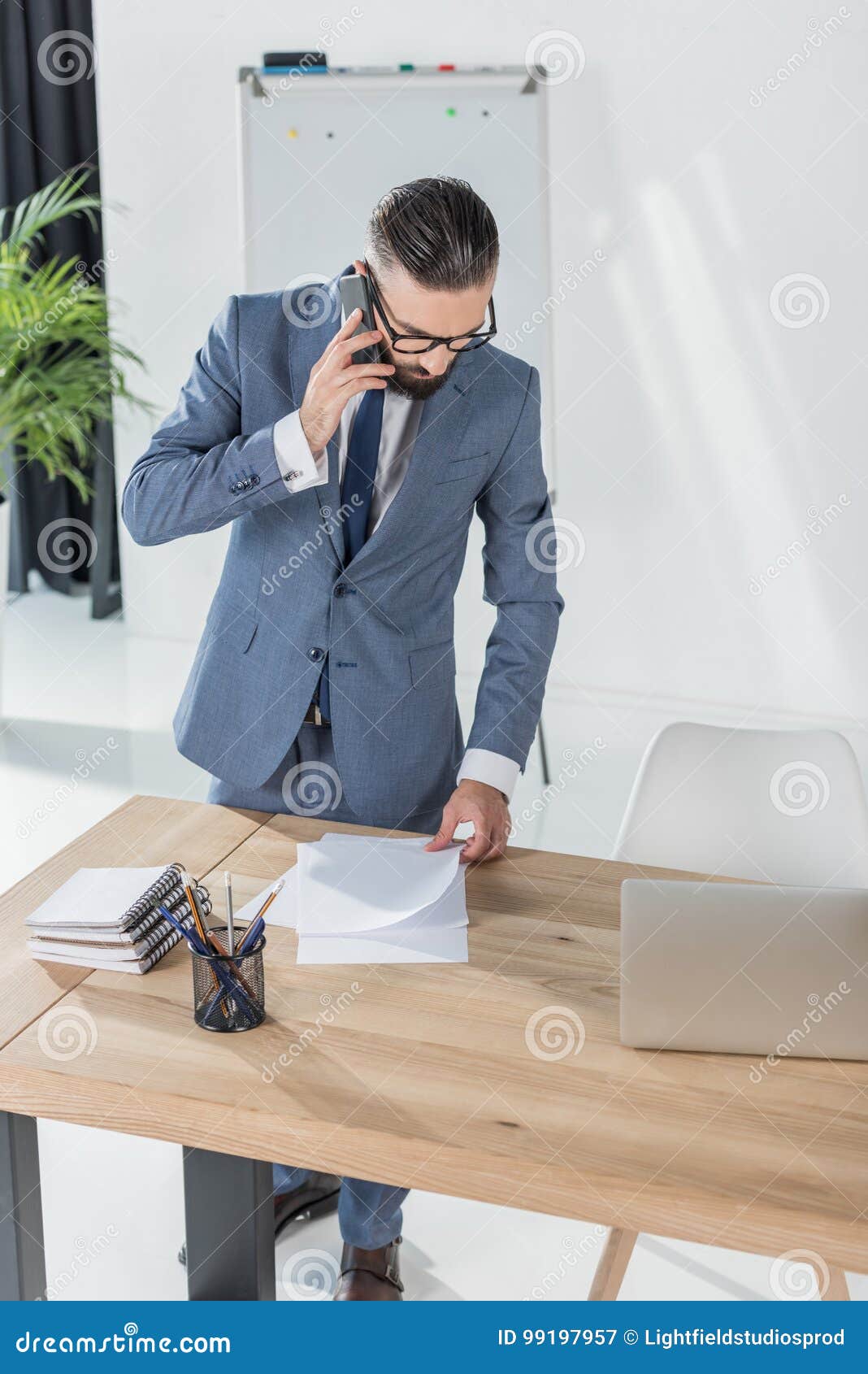Businessman Talking on Smartphone while Looking at Papers at Workplace ... Businessman Talking on Smartphone while Looking at Papers at Workplace ...