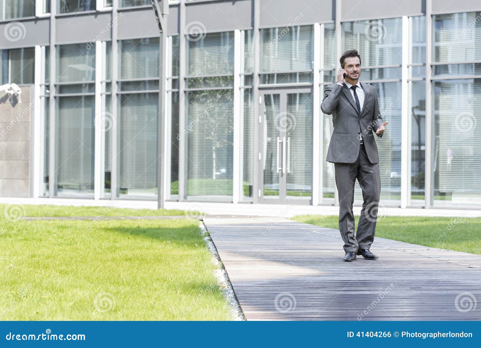 Businessman Using Cell Phone while Walking on Path Outside Office Stock ...