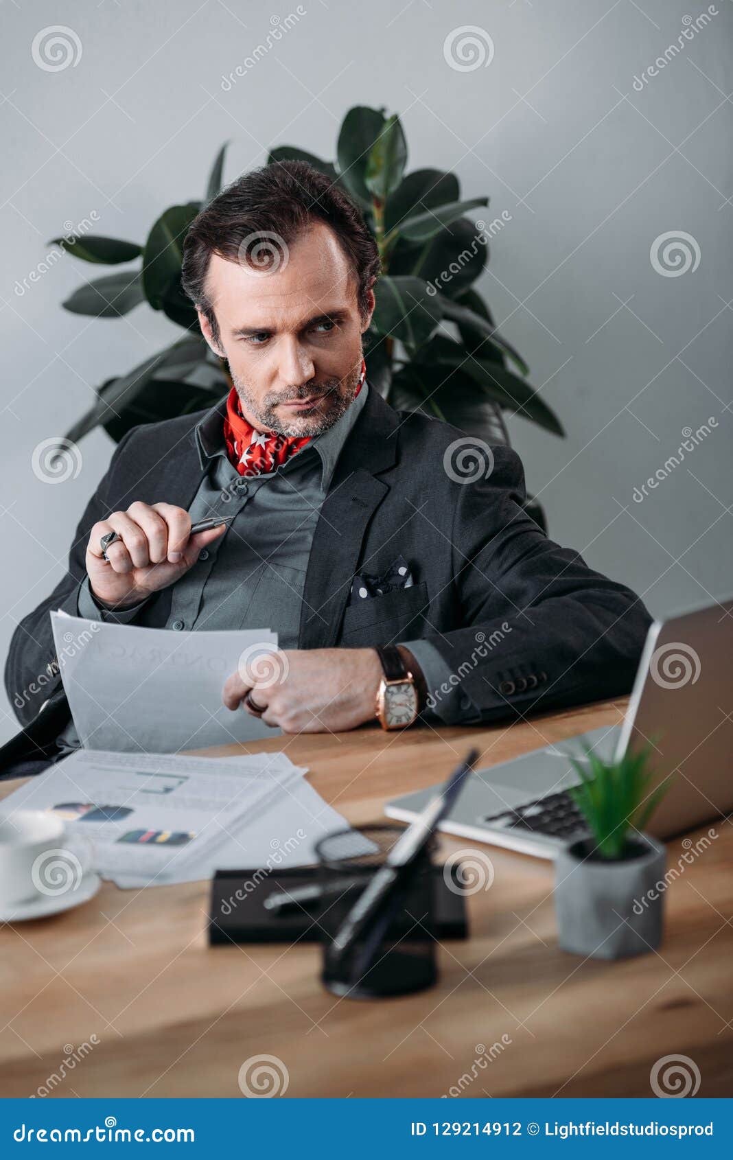 Serious Middle Aged Businessman Holding Papers and Looking at Laptop ...