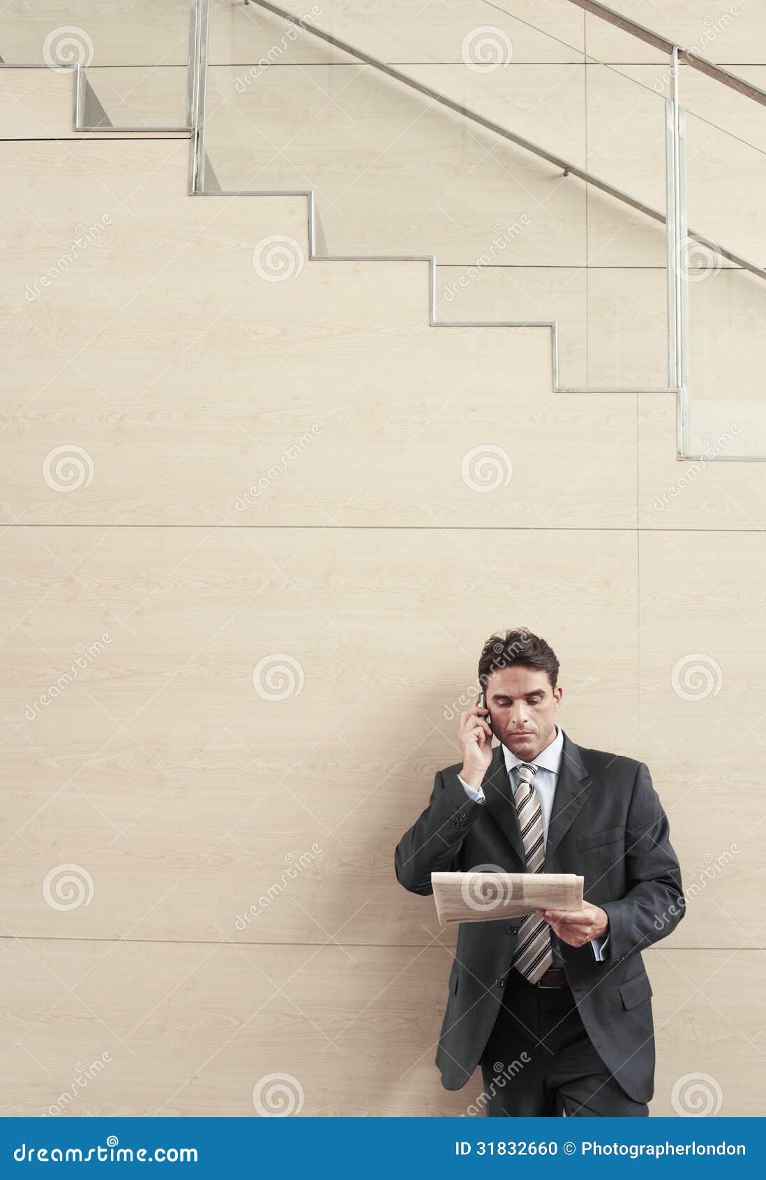 Businessman Using Mobile Phone while Reading Newspaper in Office Stock ...