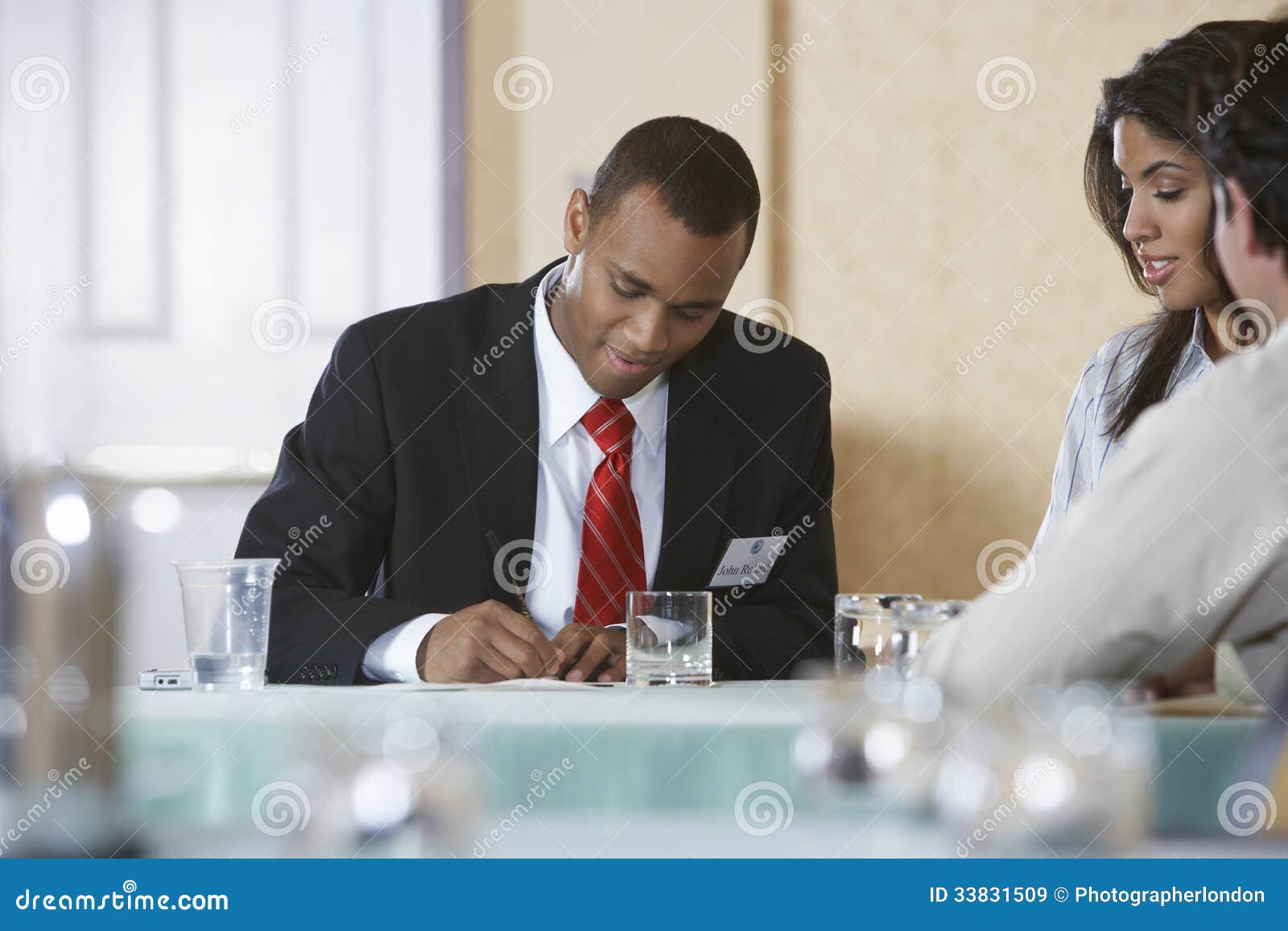 Businessman Writing on Document with Coworkers Sitting at Desk Stock ...