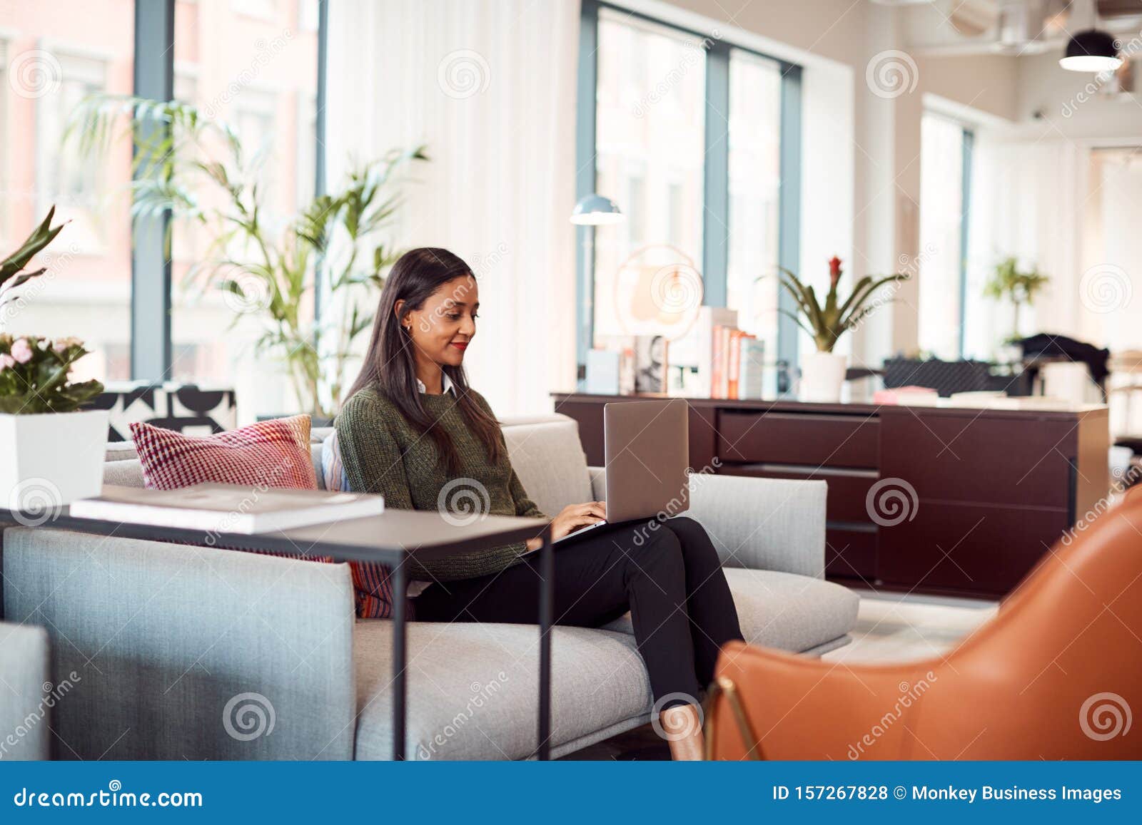 Businesswoman Sitting on Sofa Working on Laptop at Desk in Shared ...