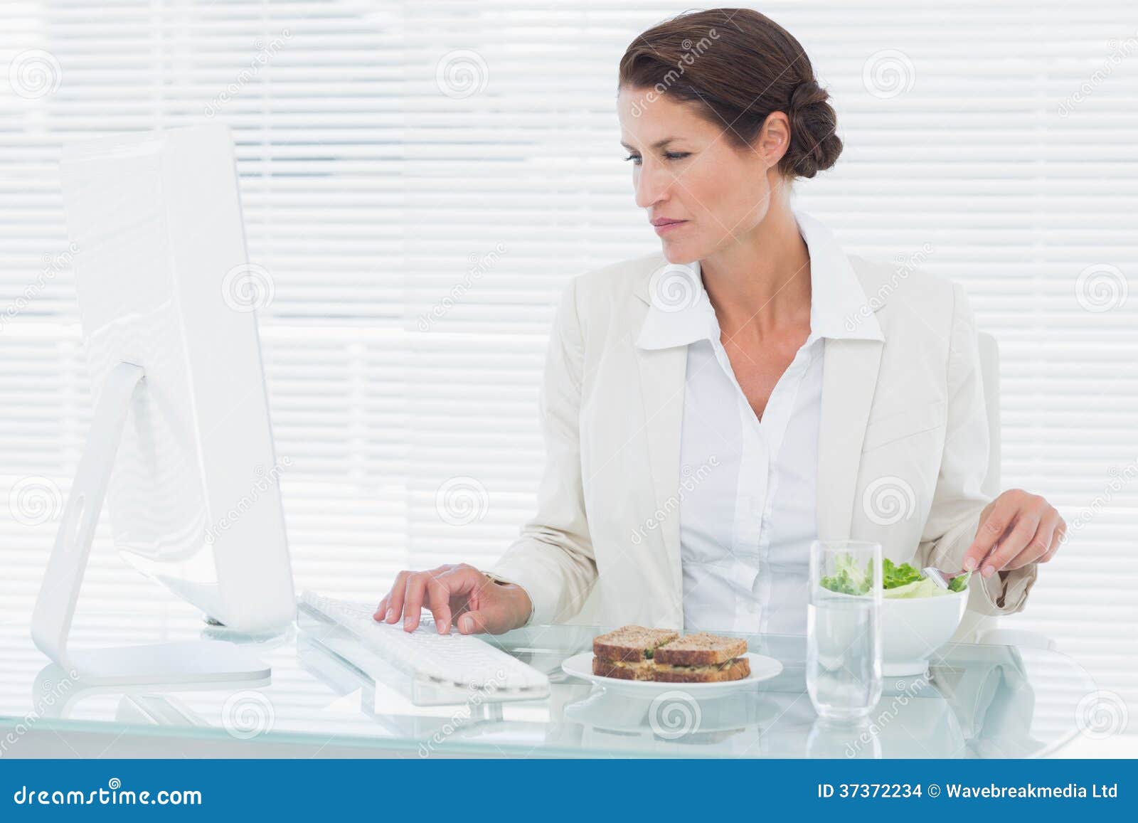 Businesswoman Using Computer while Eating Salad at Desk Stock Photo ...