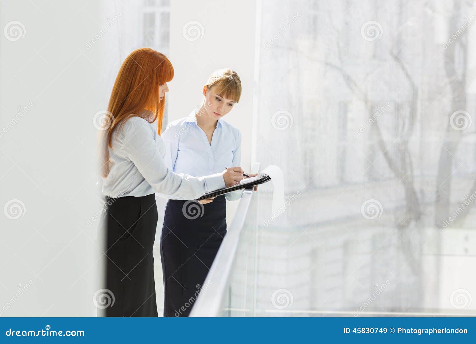 Businesswomen Doing Paperwork while Standing by Railing in Office Stock ...