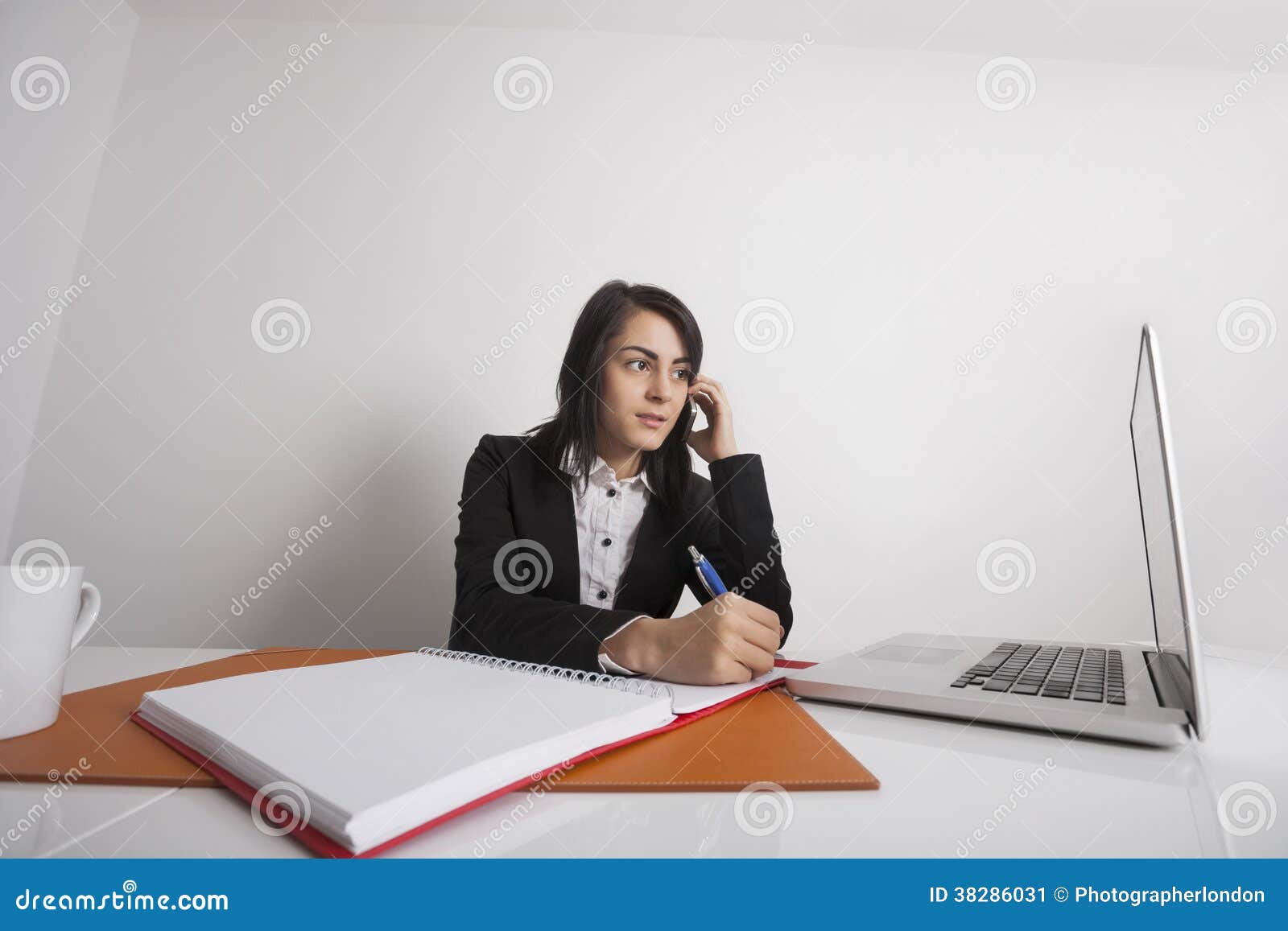 Businesswomen Using Cell Phone while Writing Notes from Laptop at ...