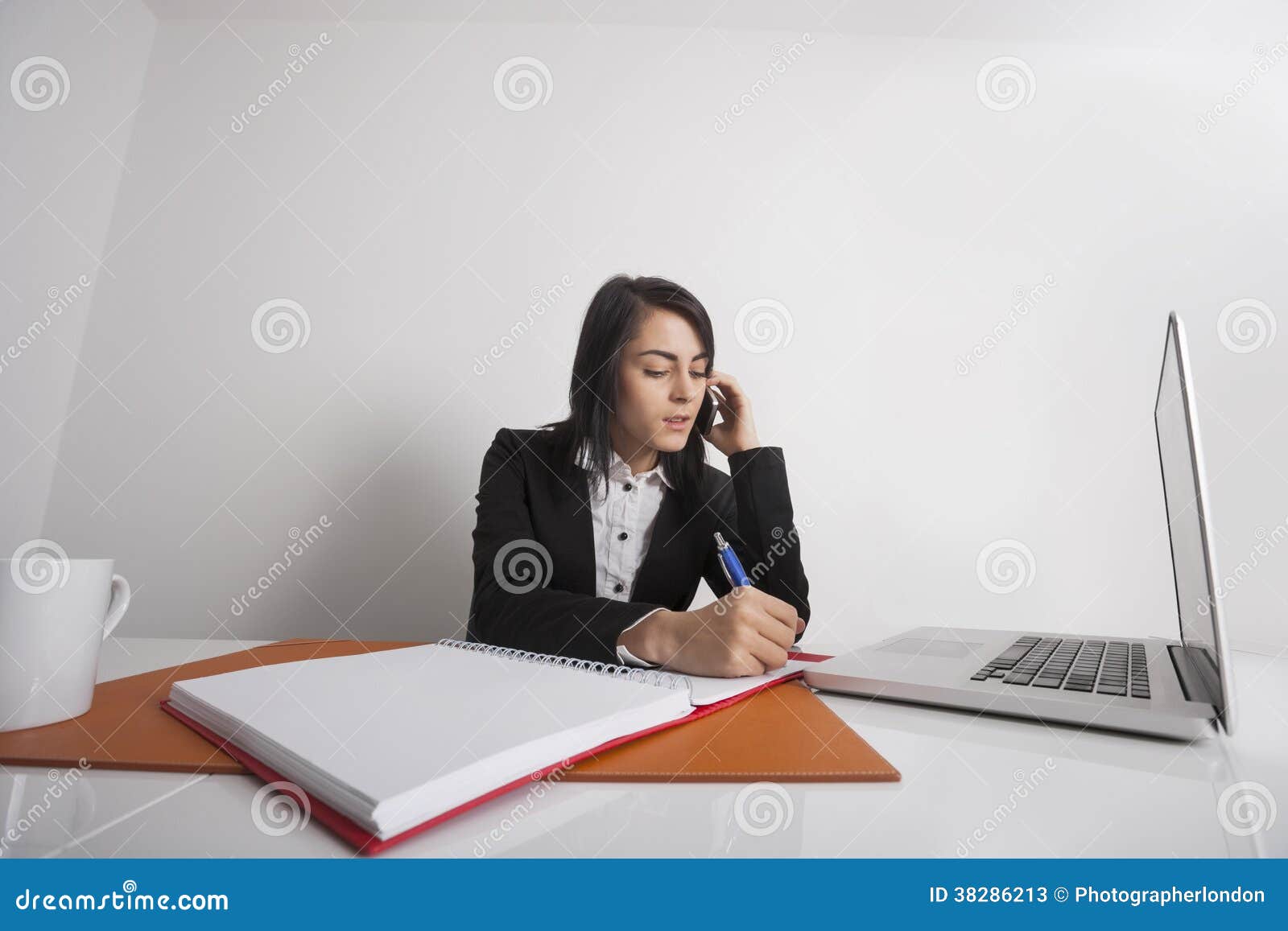 Businesswomen Writing Notes while Using Cell Phone at Office Desk Stock ...