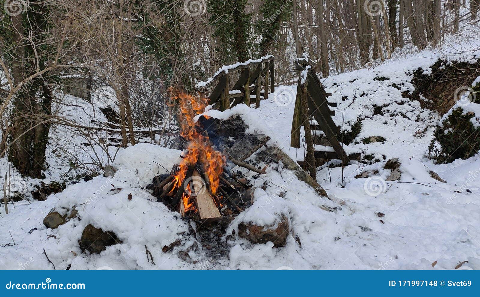Camp Fire in the Snowy Woods with a Bridge Visible in the Background ...