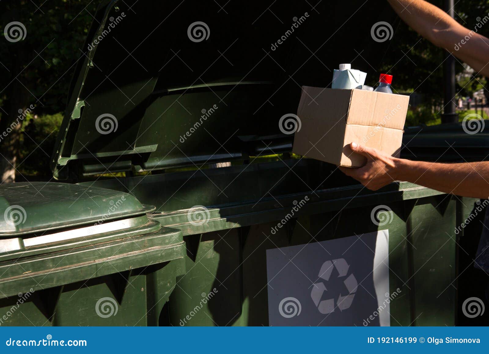 A Cardboard Box with Garbage in the Hands of a Man Near Containers for ...