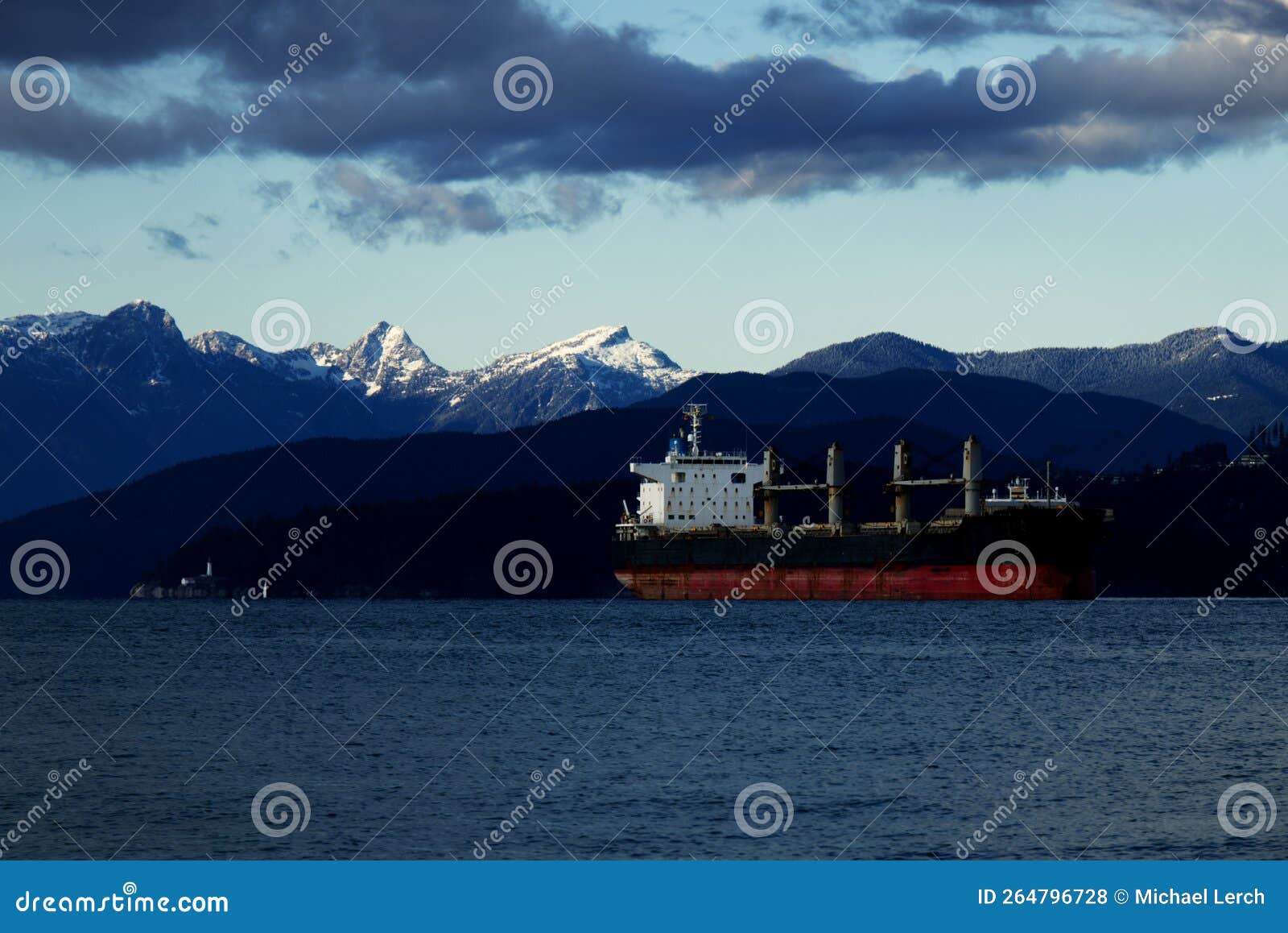 Cargo Ship in Front of Mountains with Snow Peaks and Dramatic Clouds ...