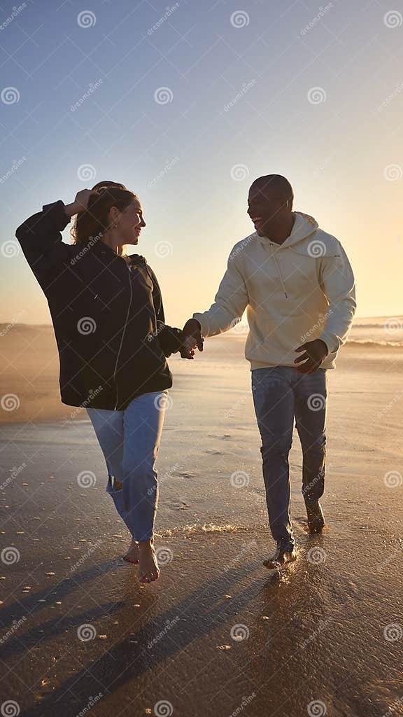 Casually Dressed Loving Young Couple Running Along Beach Shoreline