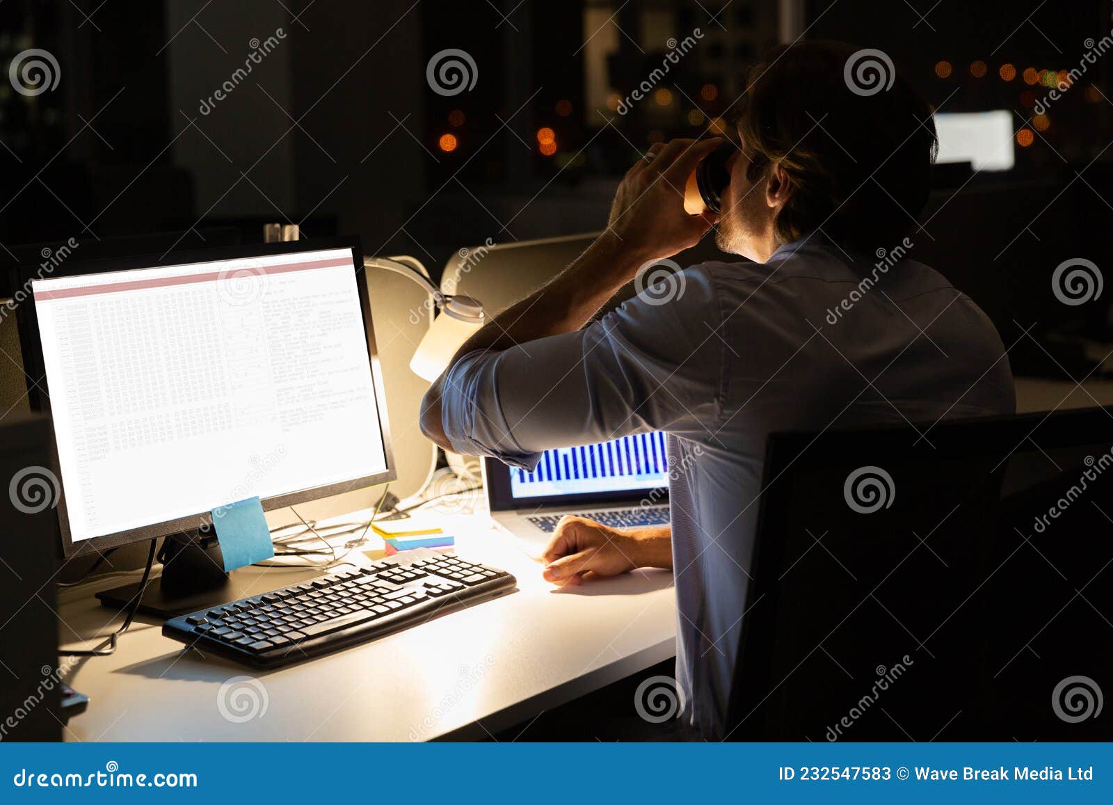 Caucasian Male Programmer Sitting At Desk Drinking Coffee Using Computer With Coding On Screen