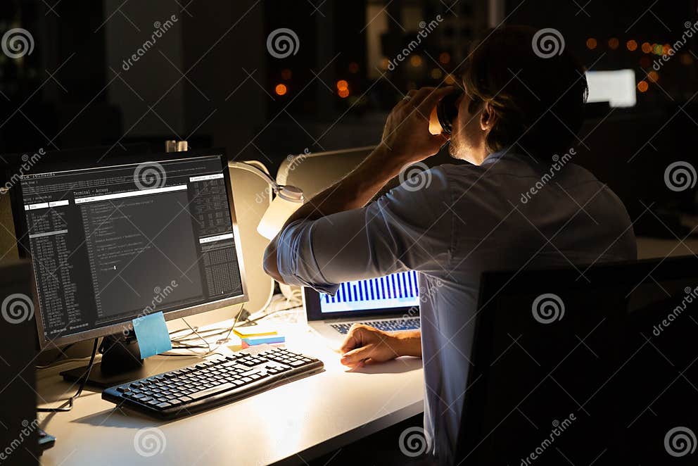 Caucasian Male Programmer Sitting at Desk, Drinking Coffee, Using Computer with Coding on Screen ...