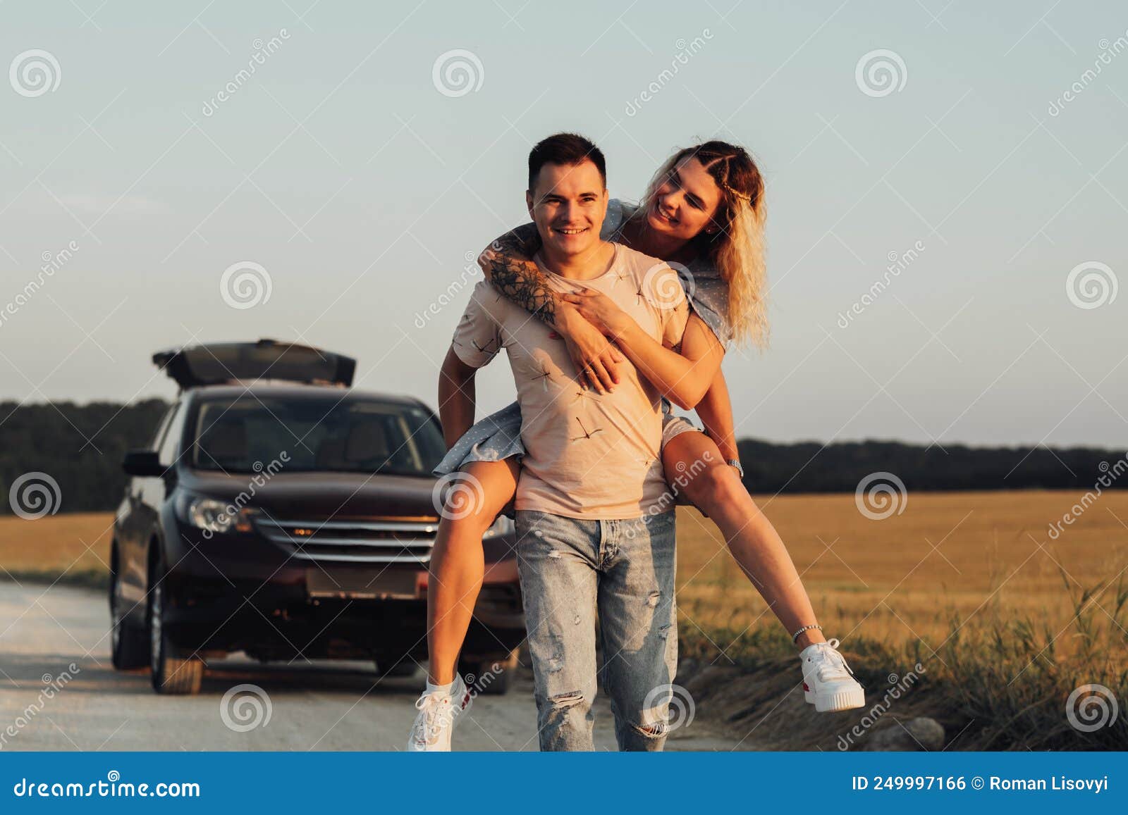 Caucasian Man Carries Girlfriend On His Back On The Background Of Their