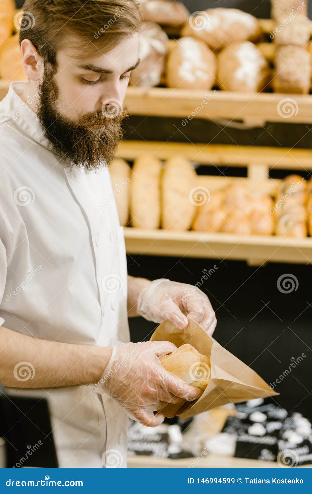 Charismatic Baker with a Beard and Mustache Puts Fresh Bread in a Paper ...