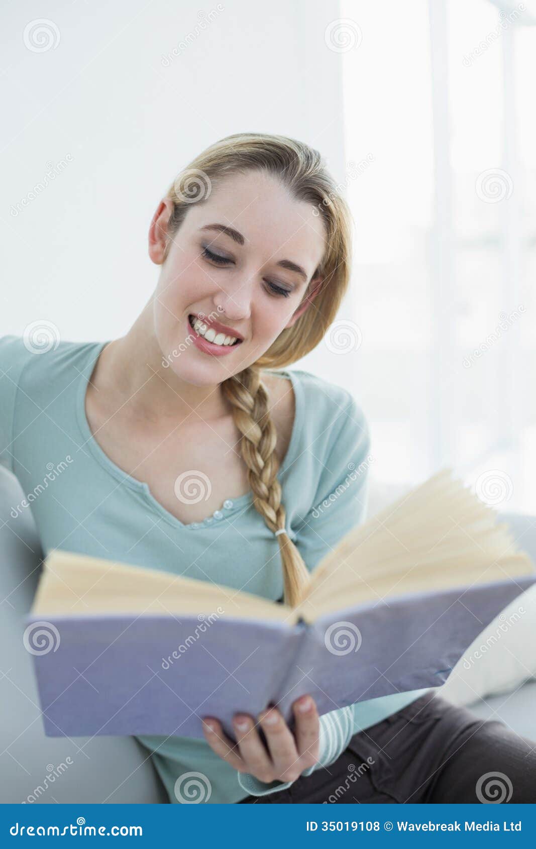Cheerful Beautiful Woman Reading A Book While Sitting On Couch Stock