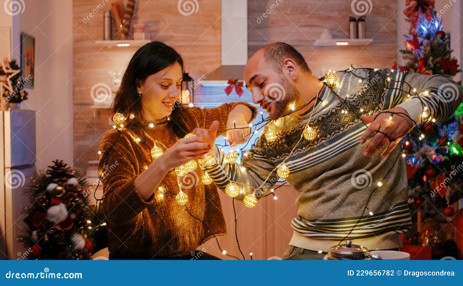 Cheerful Couple Getting Tangled in String of Twinkle Lights Stock Photo ...