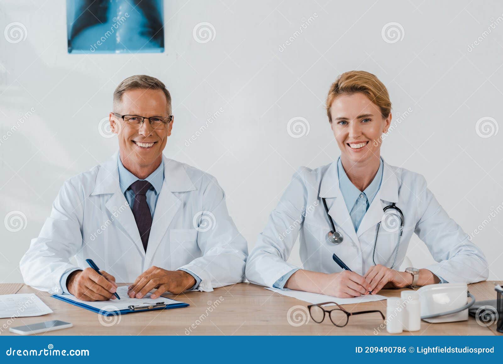 Cheerful Doctors Looking at Camera and Smiling while Sitting Near Table ...