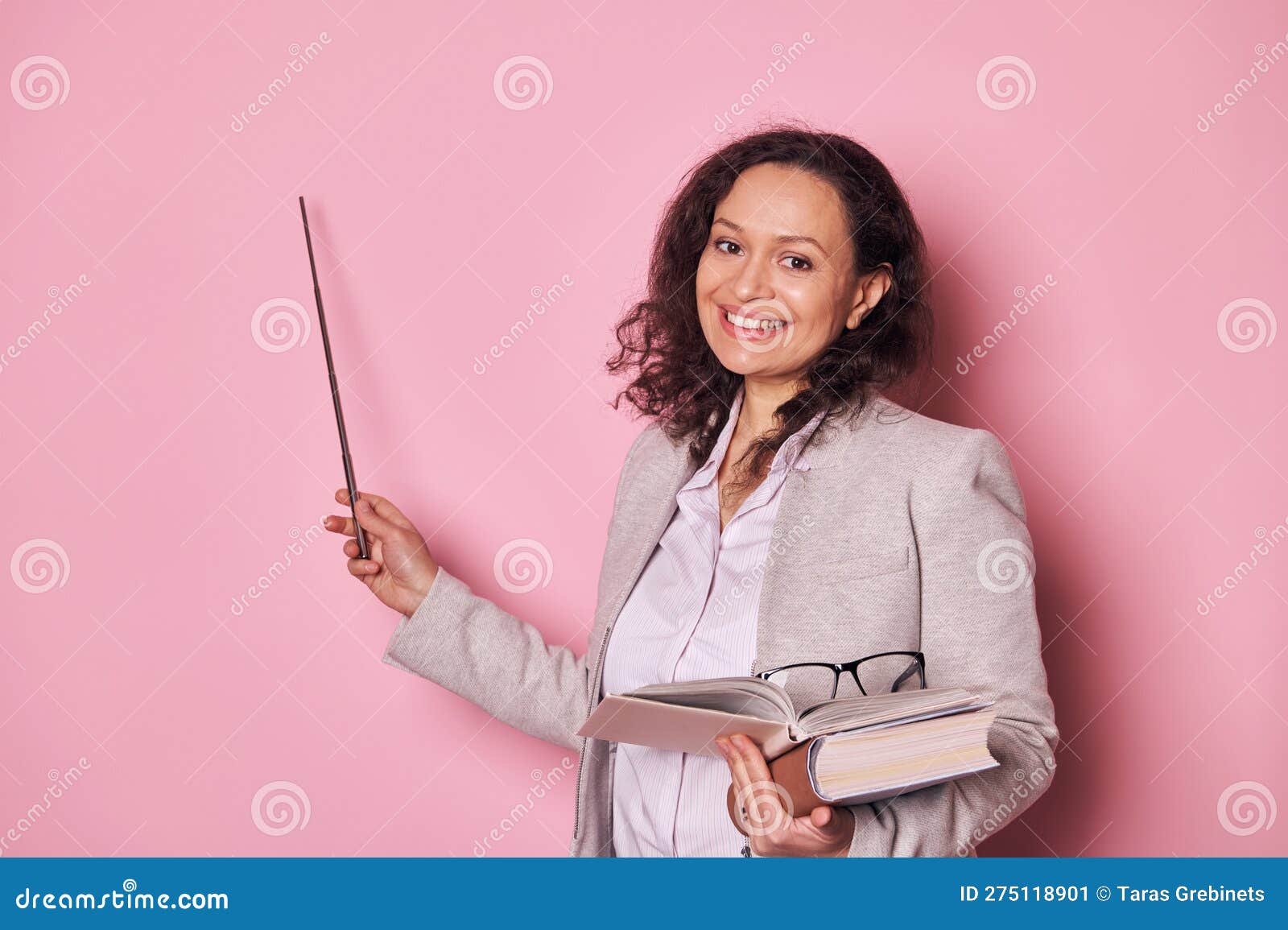 Cheerful Female Teacher Pointing with Pointer at Pink Background while ...