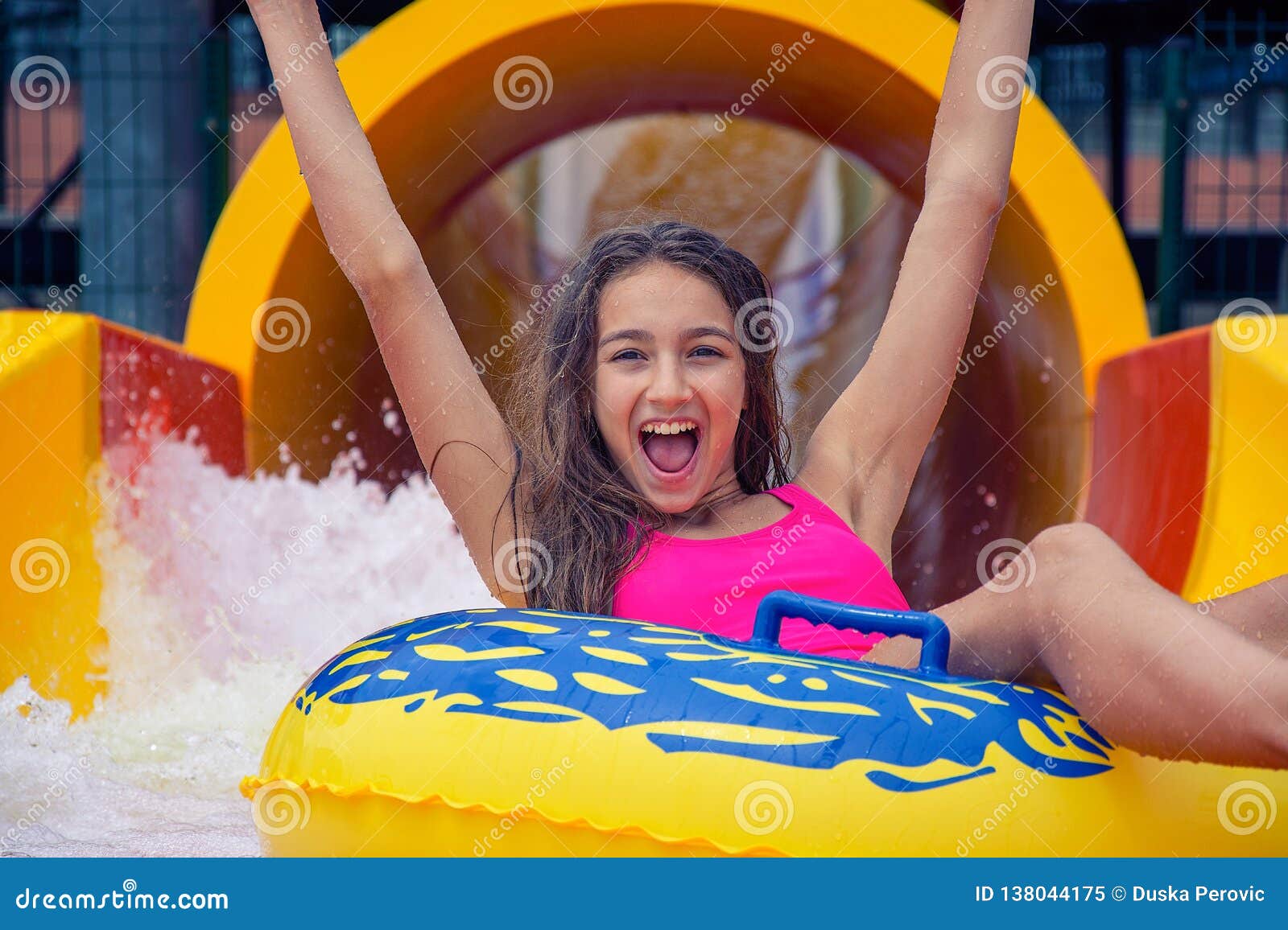 Cheerful Girl With Hands Up Having Fun Sliding In Water Park On