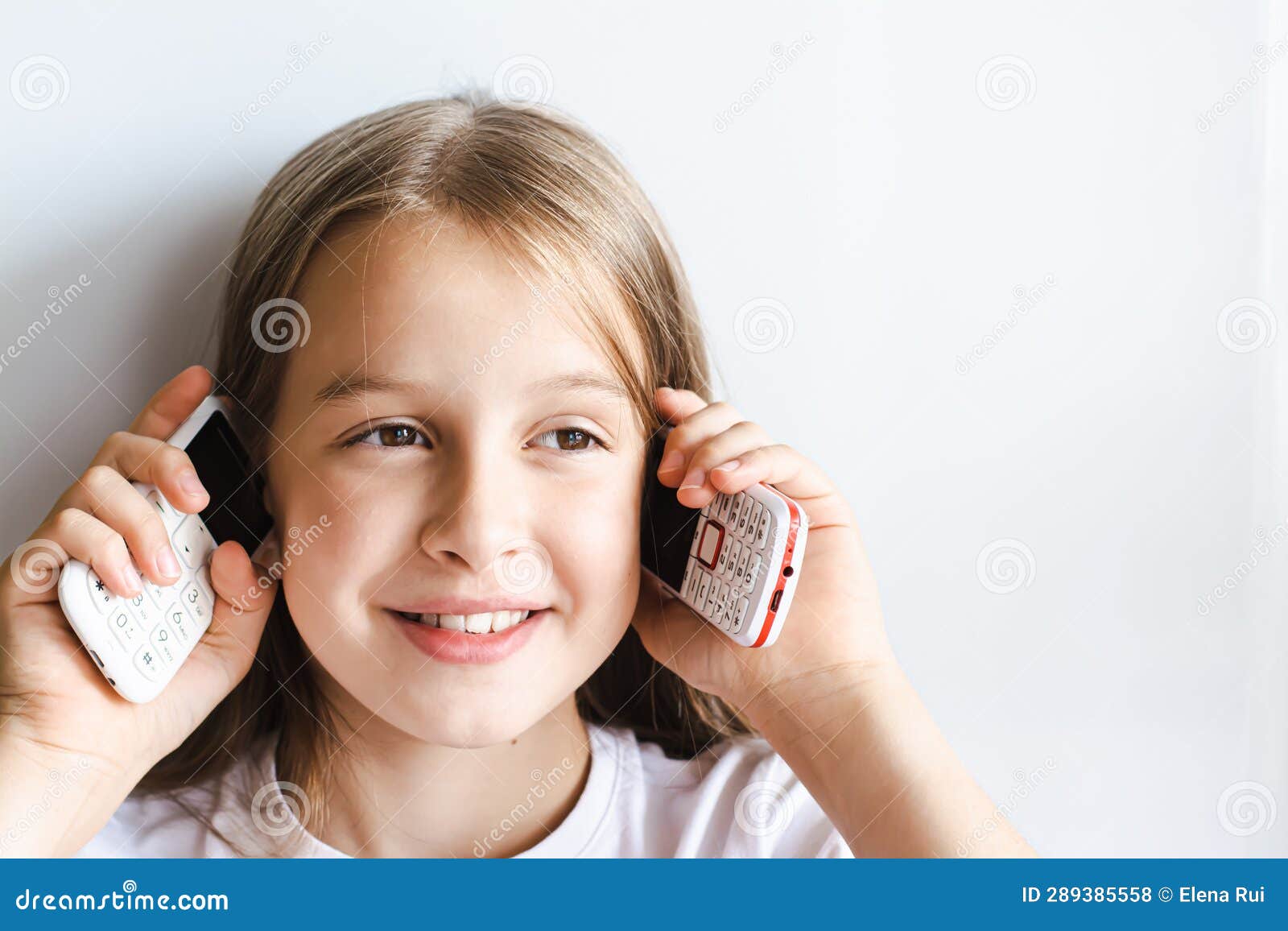 Cheerful Girl is Talking on Two Push-button Phones on a Light ...