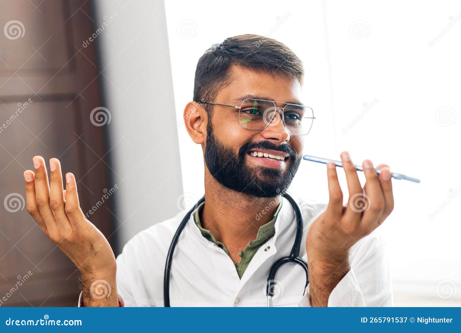 Cheerful Indian Doctor Recording a Voice Message on Mobile Phone in ... Cheerful Indian Doctor Recording a Voice Message on Mobile Phone in ...
