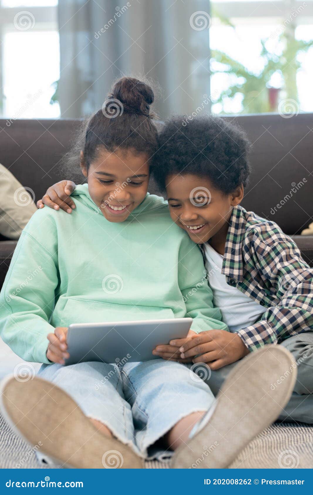 Cheerful Mixed Race Siblings Sitting On The Floor And Watching Online