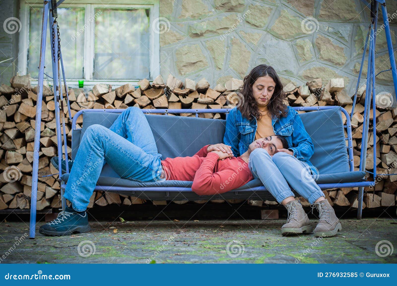 Cheerful And Romantic Couple Is Lying On A Swing Hugging And Enjoying