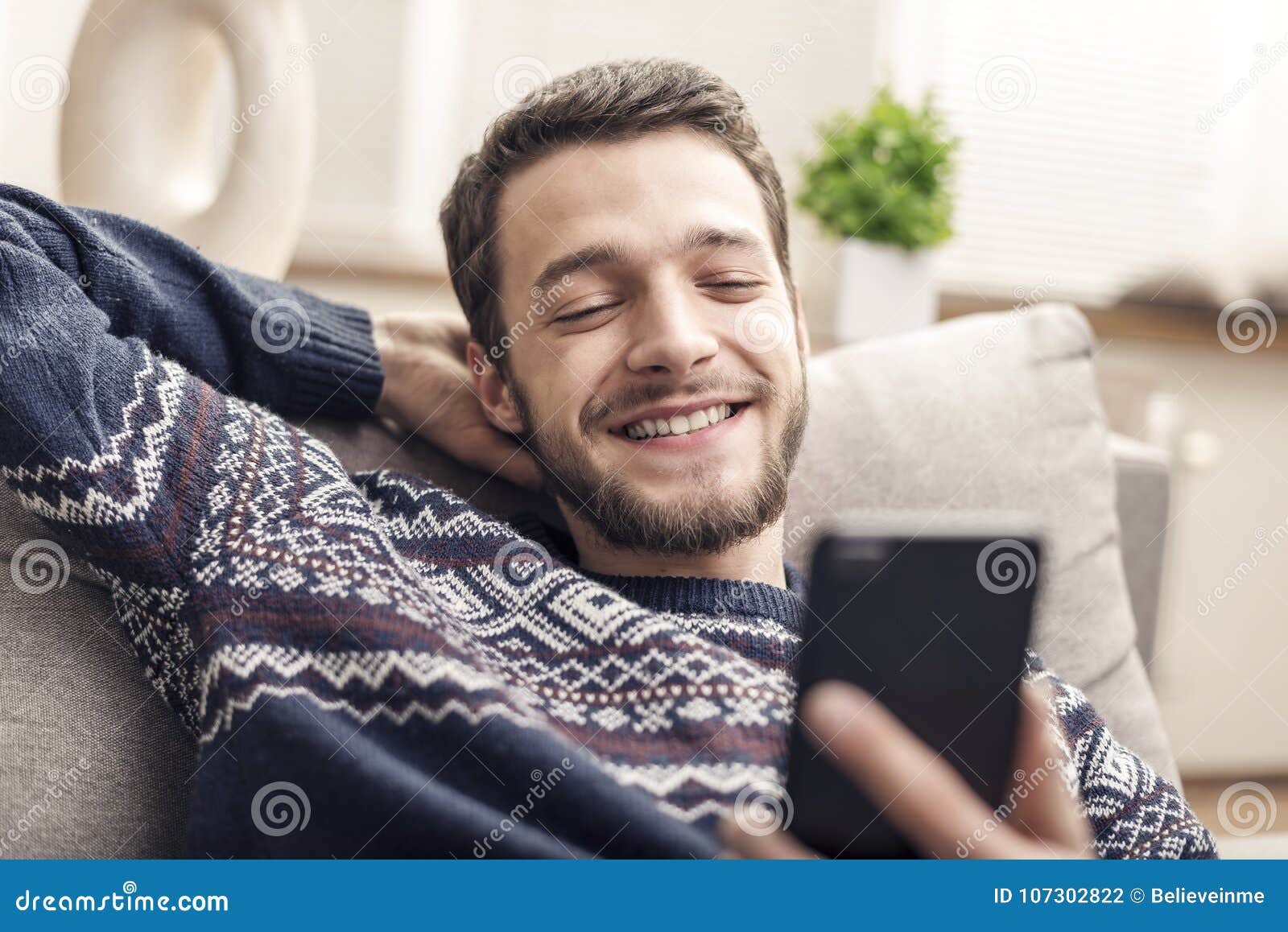 Cheerful Young Man Holding Mobile Phone and Smiling at Home. Stock ... Cheerful Young Man Holding Mobile Phone and Smiling at Home. Stock ...