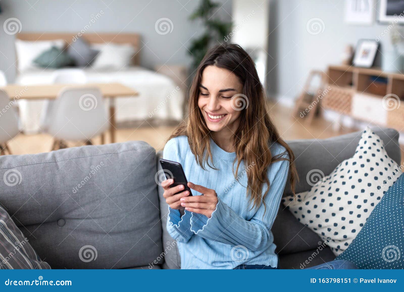 Cheerful Young Woman Using Mobile Phone while Sitting on a Couch at ...