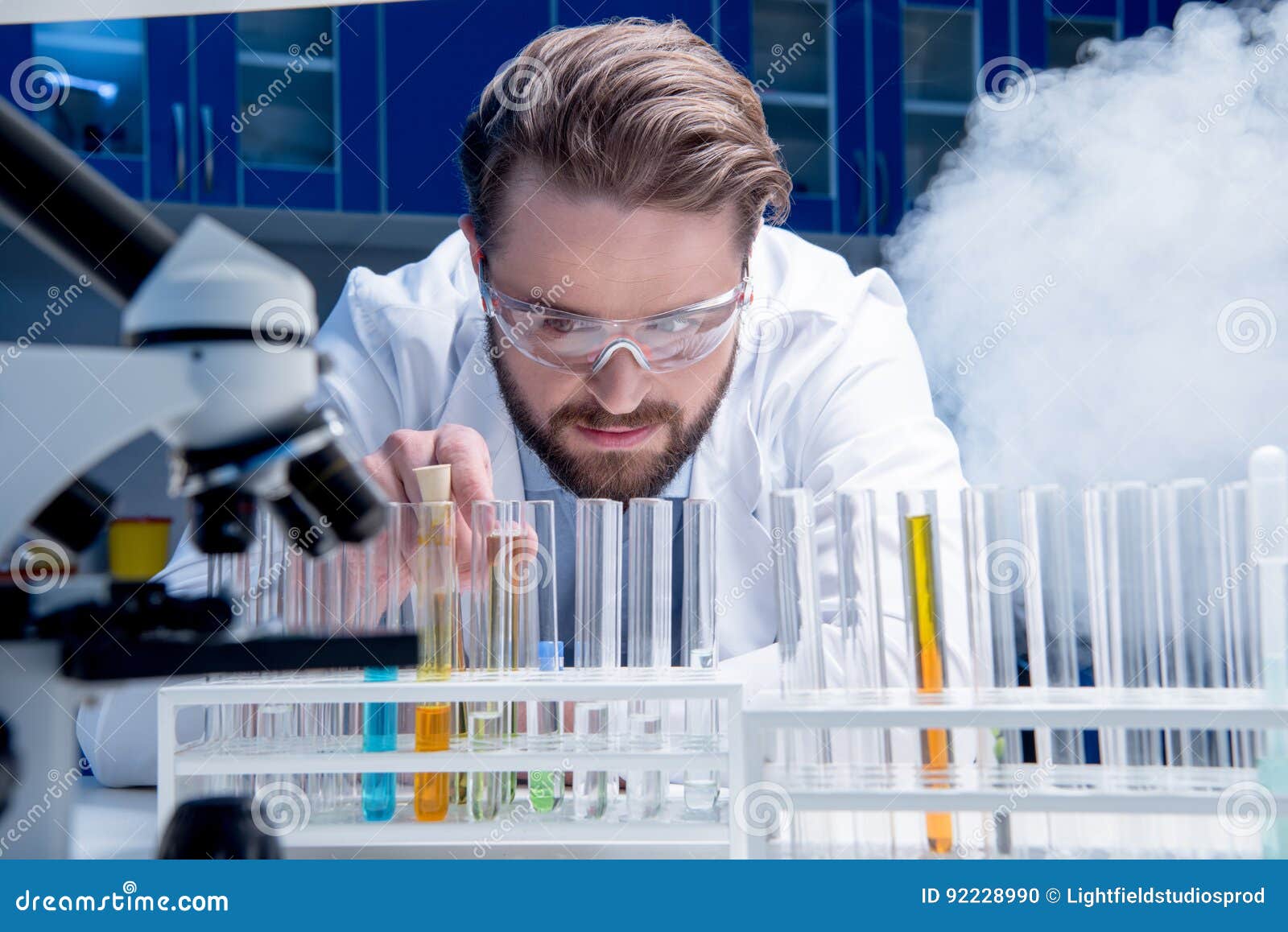 Chemist in Goggles with Reagents in Tubes and Microscope in Laboratory ...