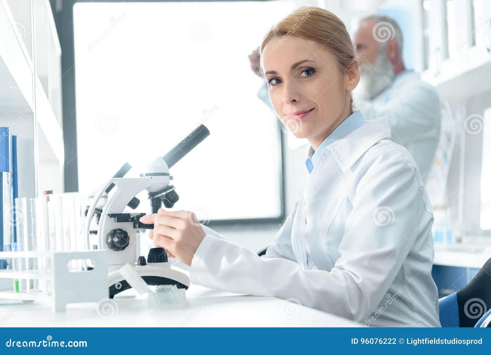 Chemist in White Coat Working with Microscope and Reagents while ...