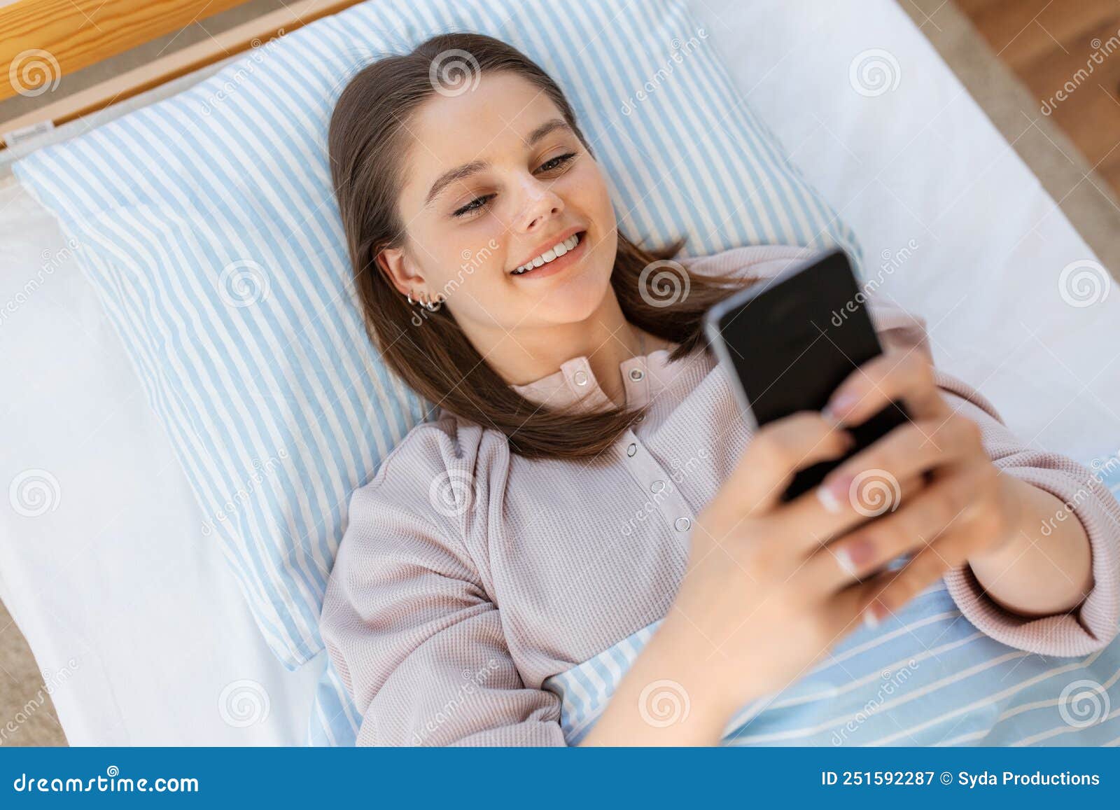 Chica Feliz Con Smartphone En La Cama En Casa Imagen De Archivo