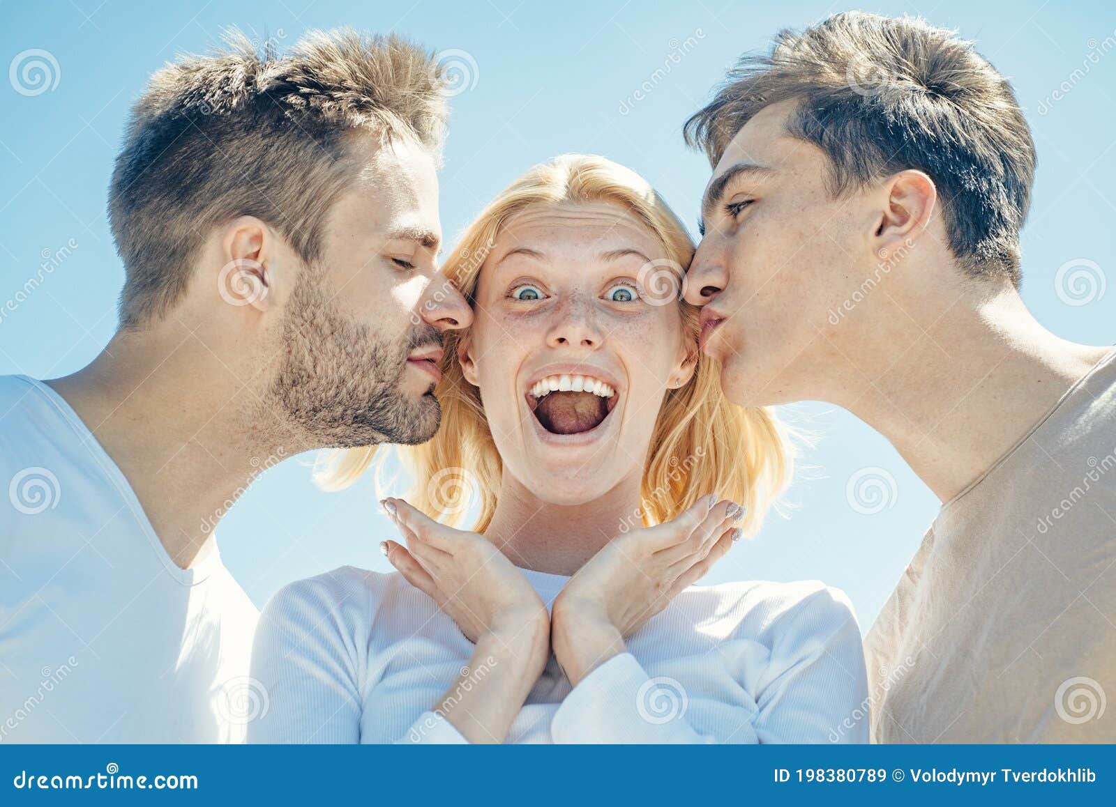 Chica Rubia Y Feliz Recibiendo Besos De Dos Chicos Guapos Encantadora Mujer Parada Entre Dos
