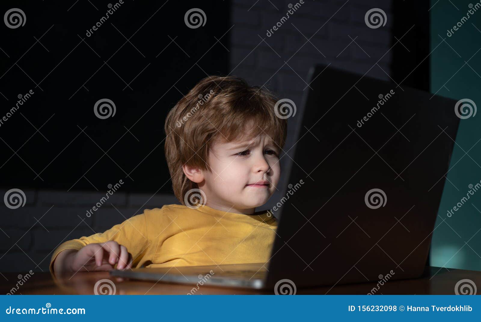 Child is Bored at the Computer at Night in the Dark. Seated Child Using ...