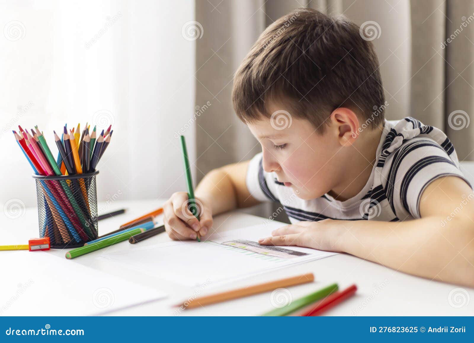A Child Boy Draws on White Paper with Colored Pencils while Sitting at ...