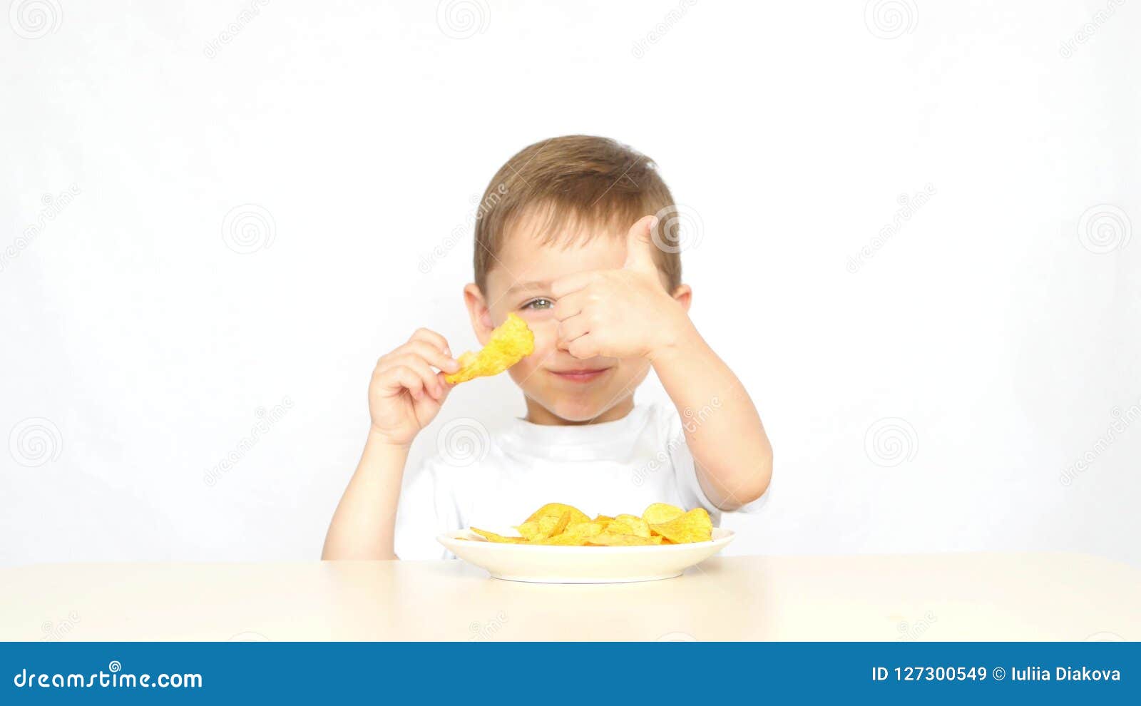 A Child with Pleasure Eating Potato Chips Sitting at a Table on a White ...