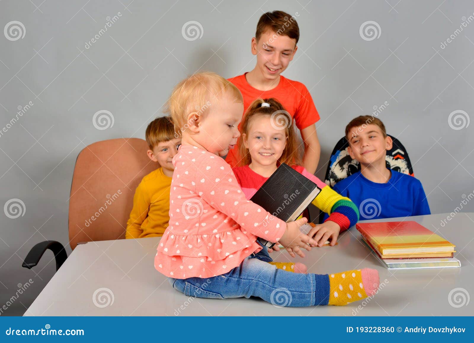 The Child is Sitting on the Table with a Serious Face and with a Book ...
