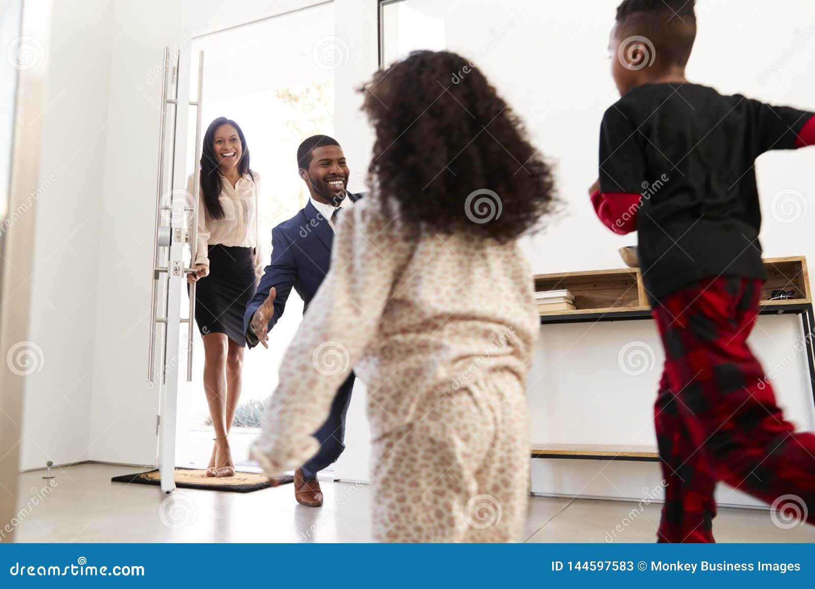 Children Greeting and Hugging Working Parents As they Return Home from ...