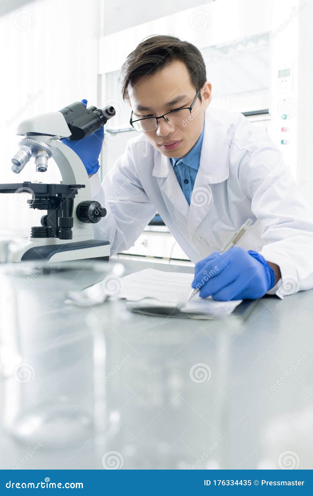 Chinese Male Lab Worker in Gloves and Whitecoat Making Notes in Notepad ...