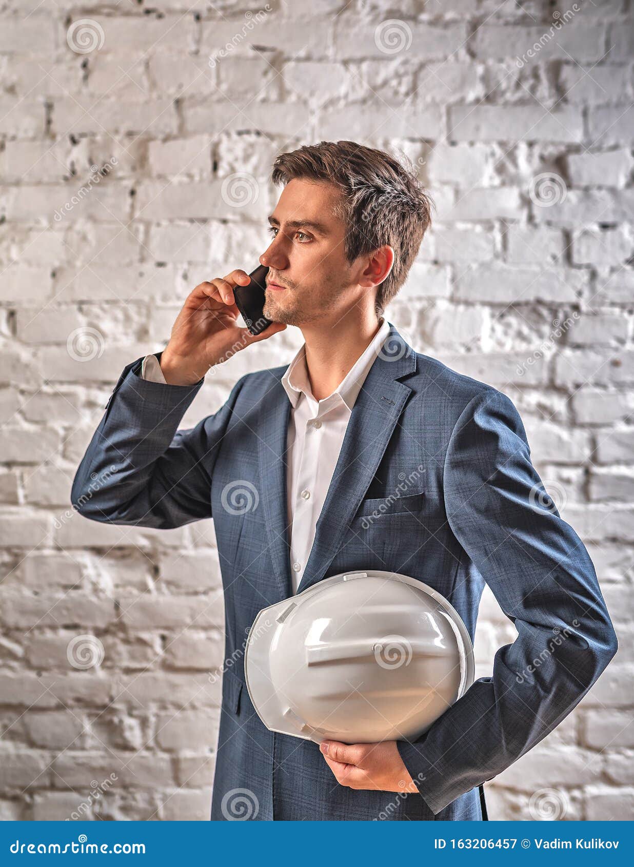 Civil Engineer In A White Helmet With Documents In His Hands Talking On ...