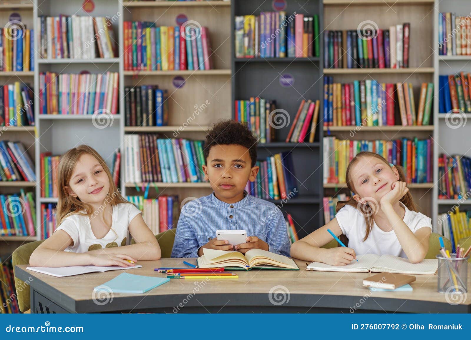 Multi-ethnic Pupils Study and Write at Table in Library or Classroom ...