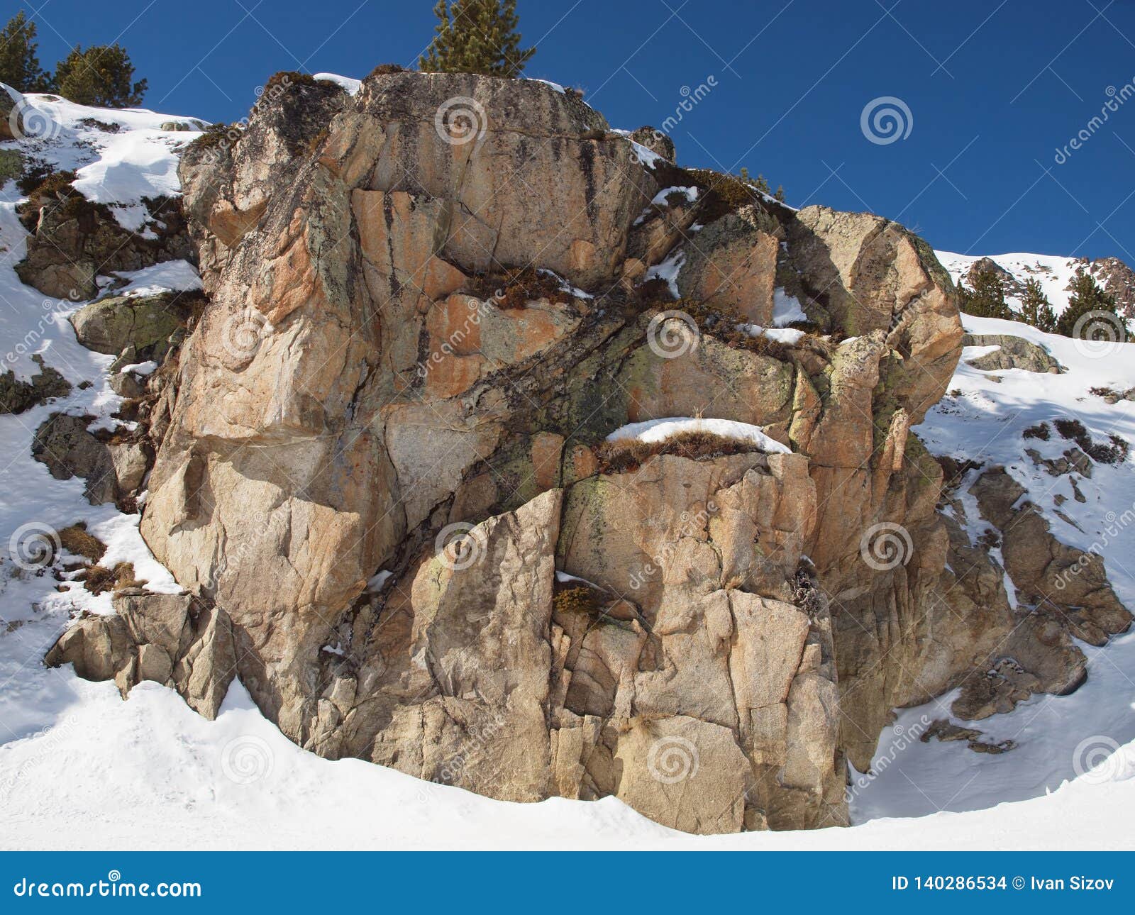 A Cliff on a Snowy Slope Against the Blue Sky with a Lone Tree on Top ...