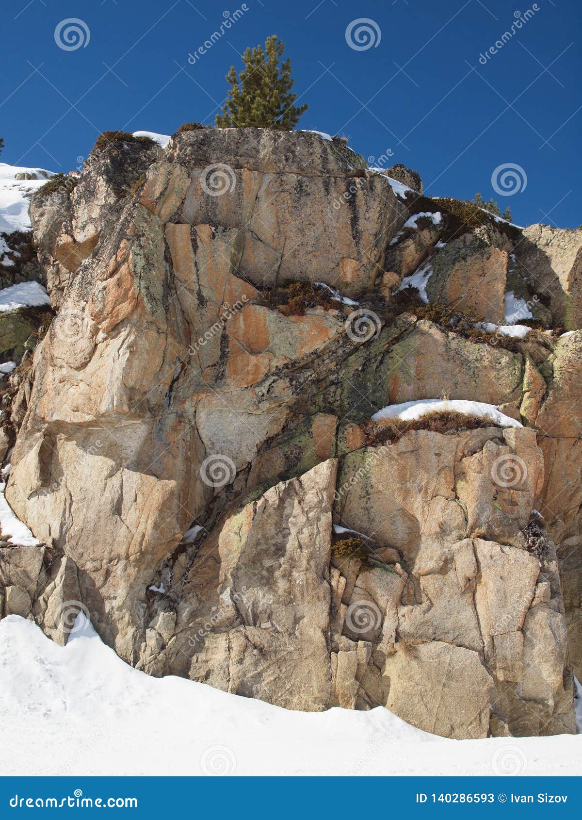 A Cliff on a Snowy Slope Against the Blue Sky with a Lone Tree on Top ...